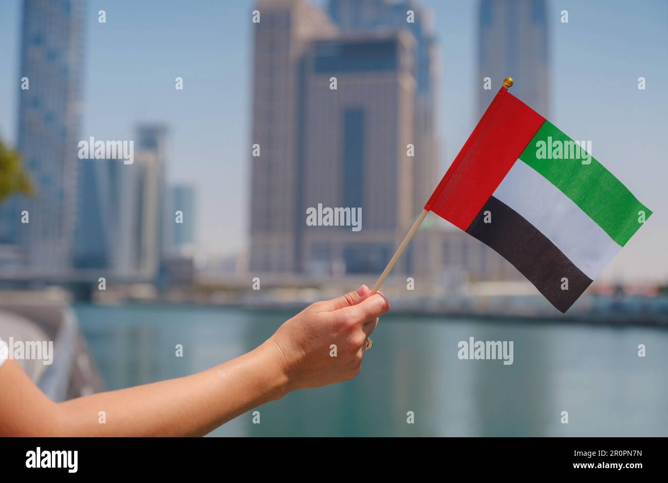Close up of a female hand holding tiny flag of UAE against Dubai ...