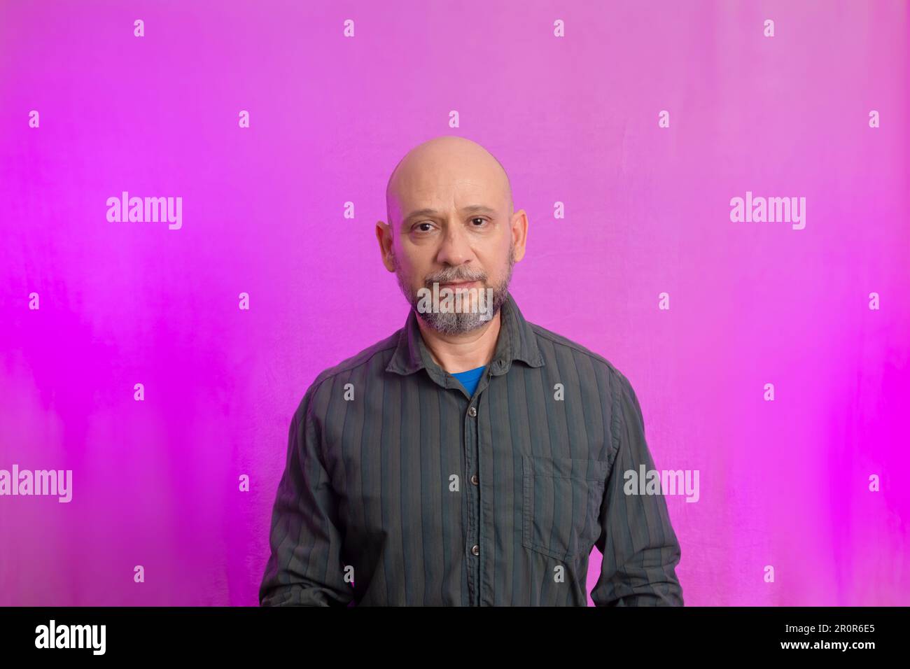 Portrait of a serious 50-year-old man with a beard and bald head. Isolated on pink background ...