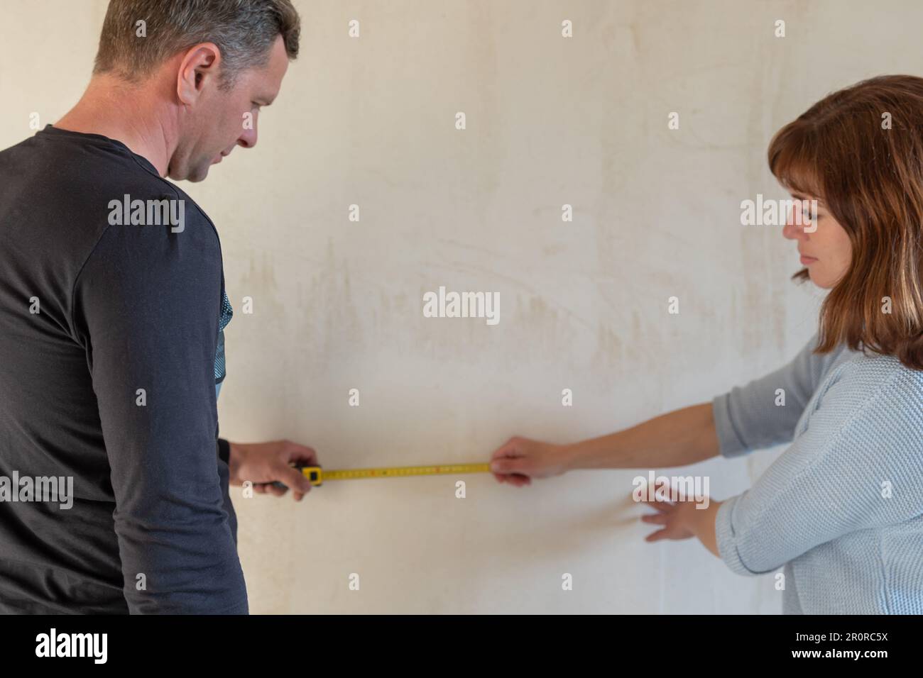 Young couple moving in new apartmen. People measure size of wall with ...
