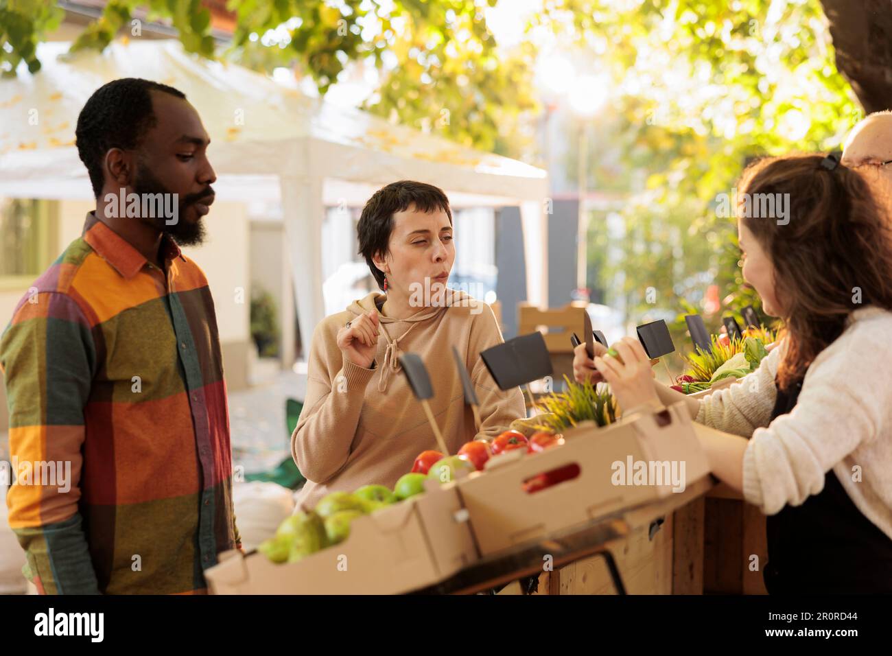 Young customers tasting free food samples at farmers market, fresh juicy fruits and vegetables ...