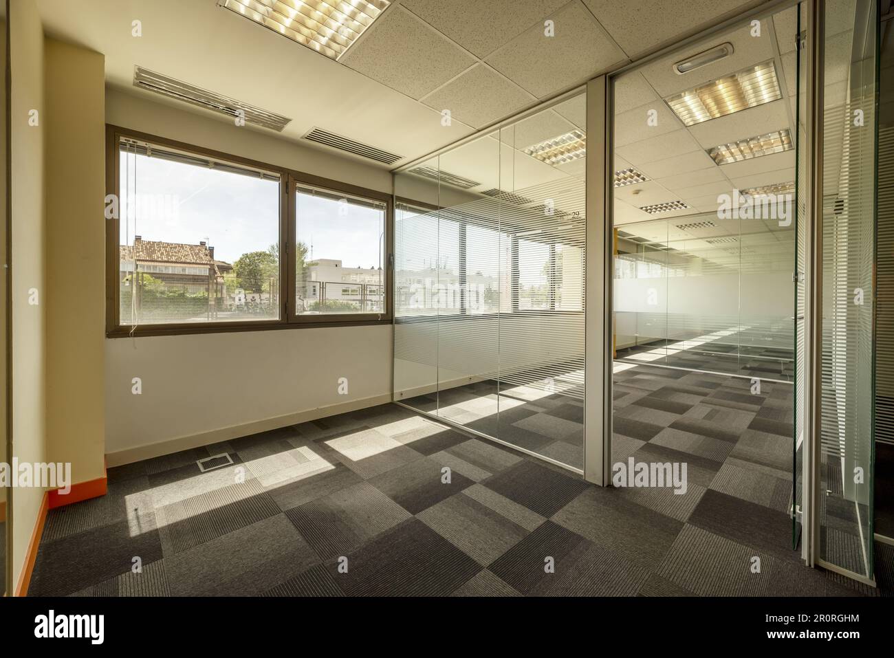 Empty offices with glass partitions, carpeted floors and windows along ...