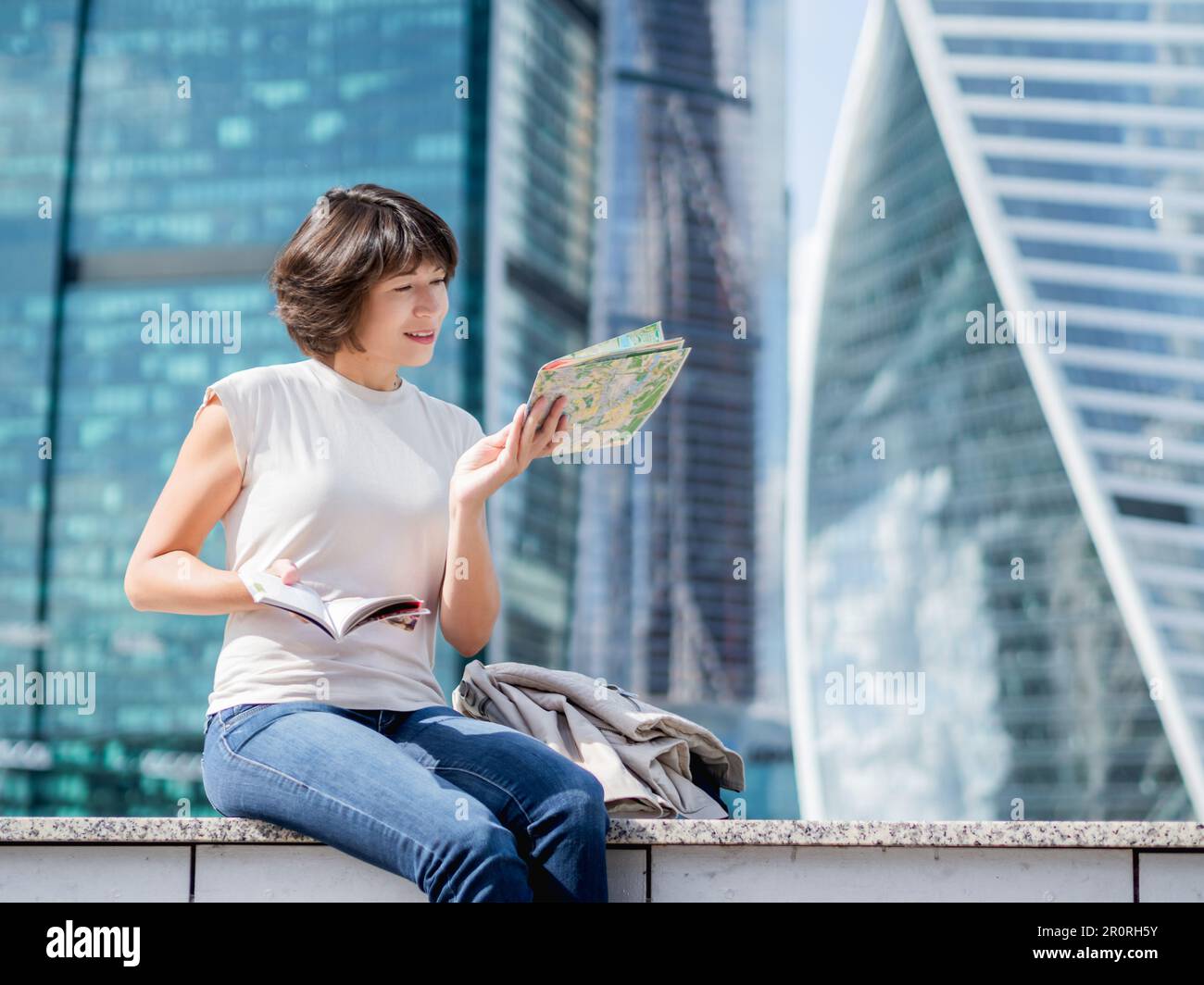 Smiling woman is reading paper map sitting on background of buildings ...