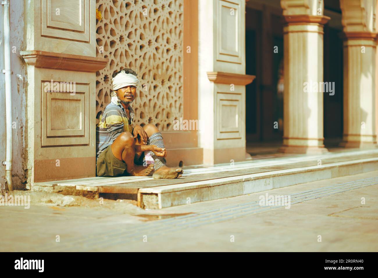 A man in a state of destitution, wearing tattered clothing, sitting on ...