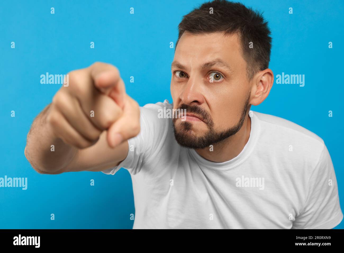 Aggressive man pointing on light blue background Stock Photo - Alamy