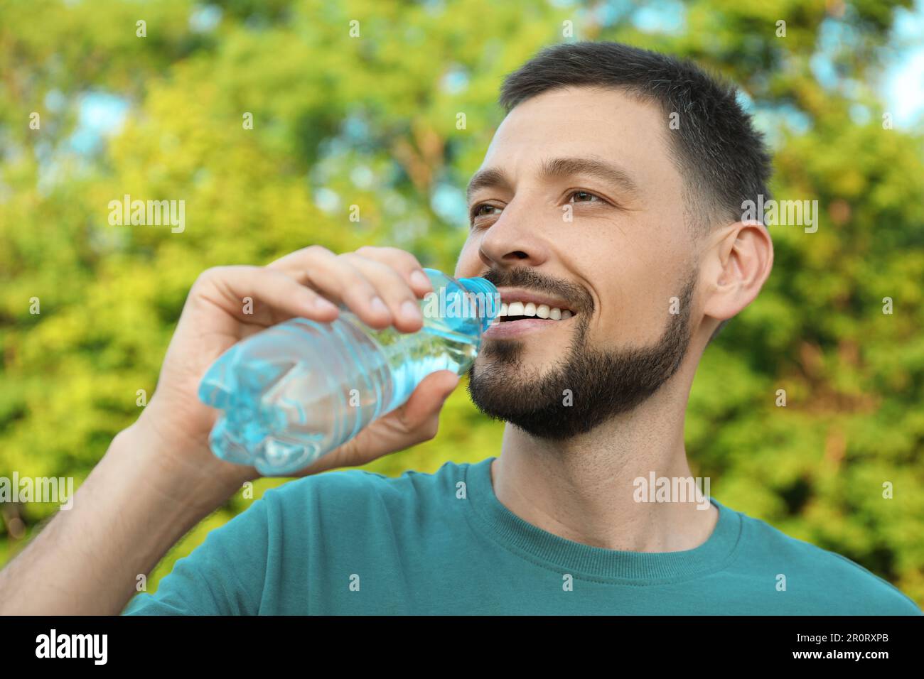 Happy man drinking water outdoors on hot summer day. Refreshing drink ...