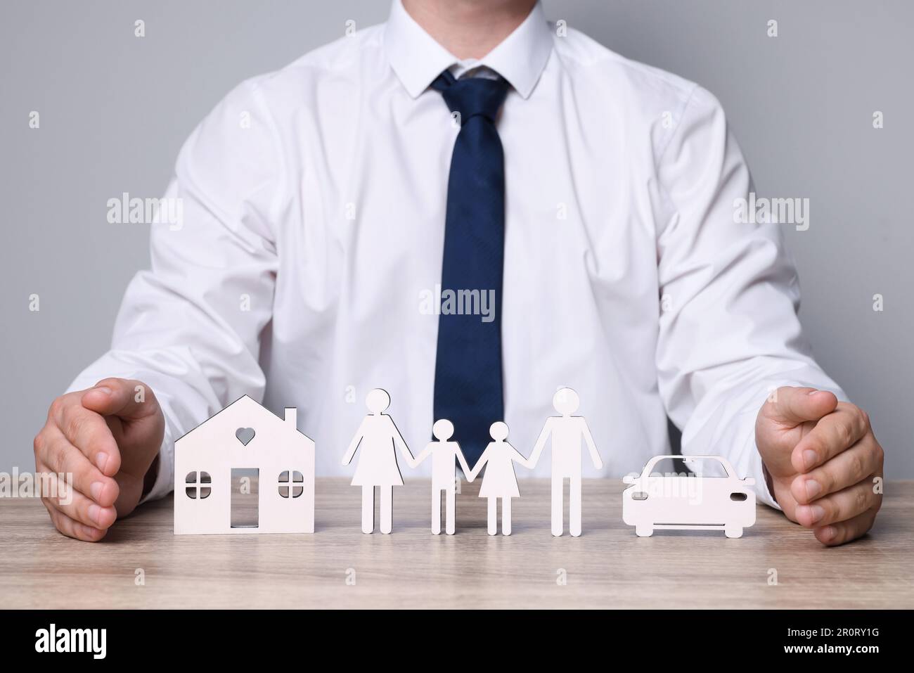 Man protecting figures of family, car and house at wooden table ...