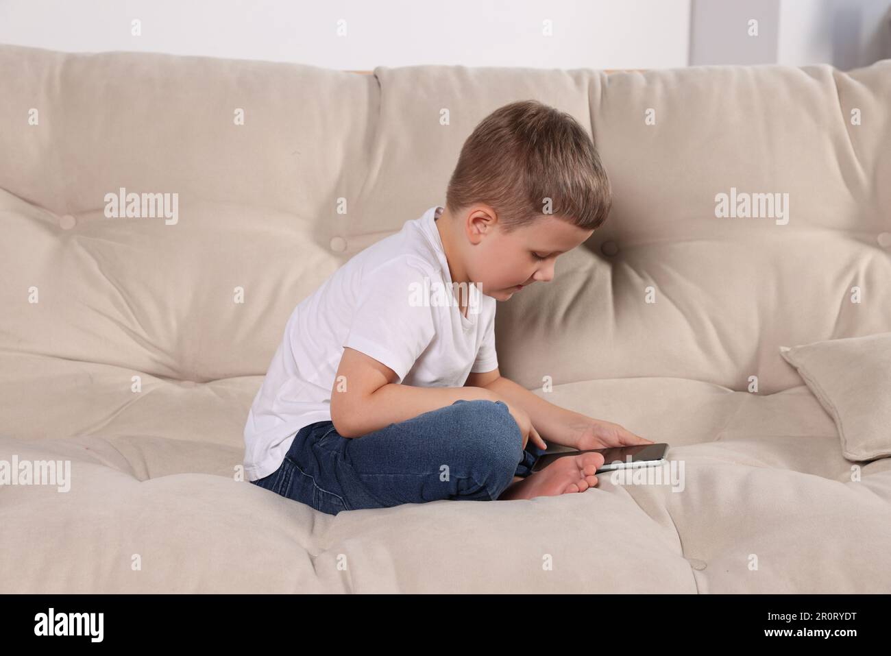 Boy with poor posture using phone on beige sofa indoors. Symptom of ...