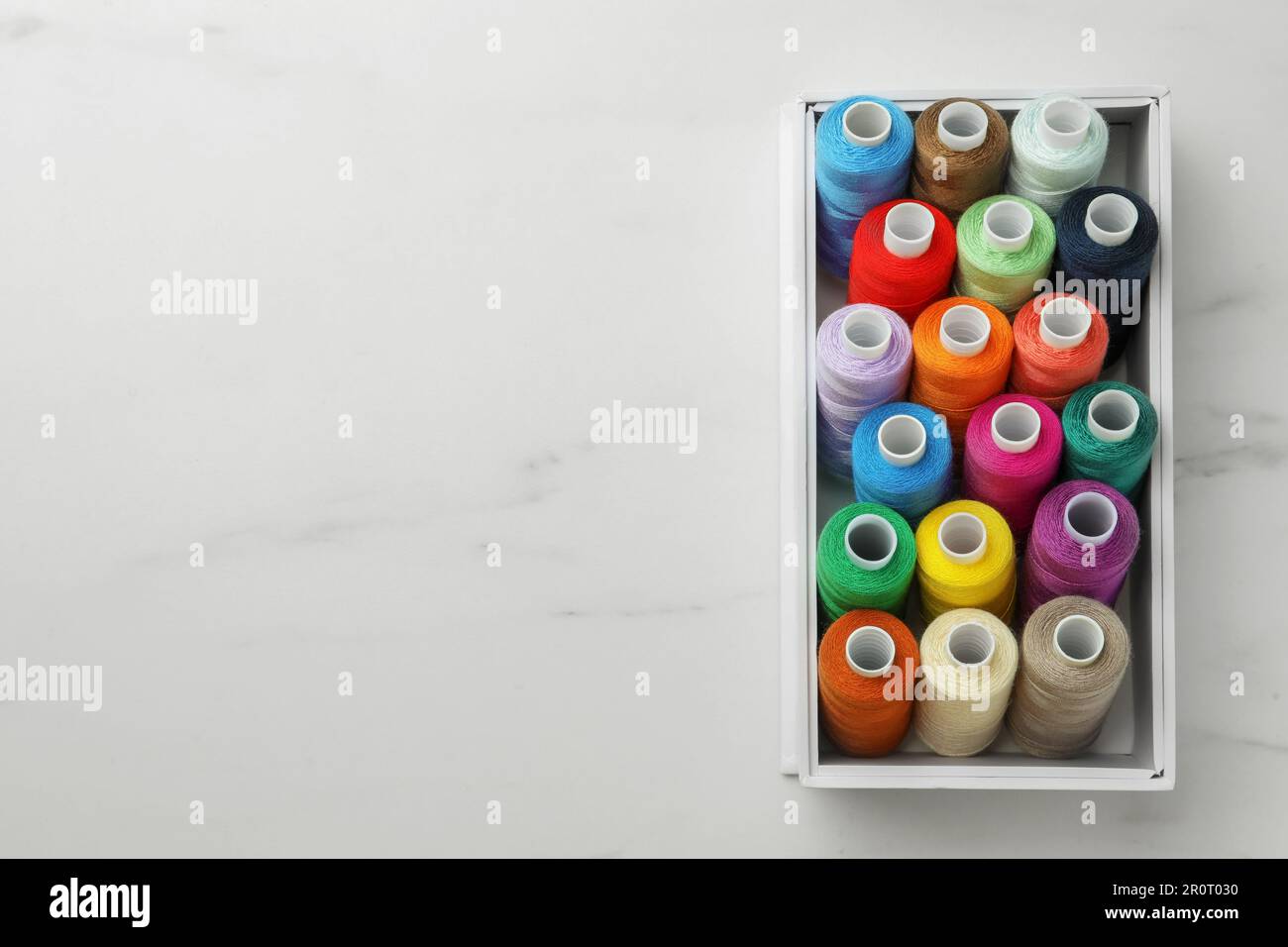 Box with colorful sewing threads on white marble table, top view. Space ...