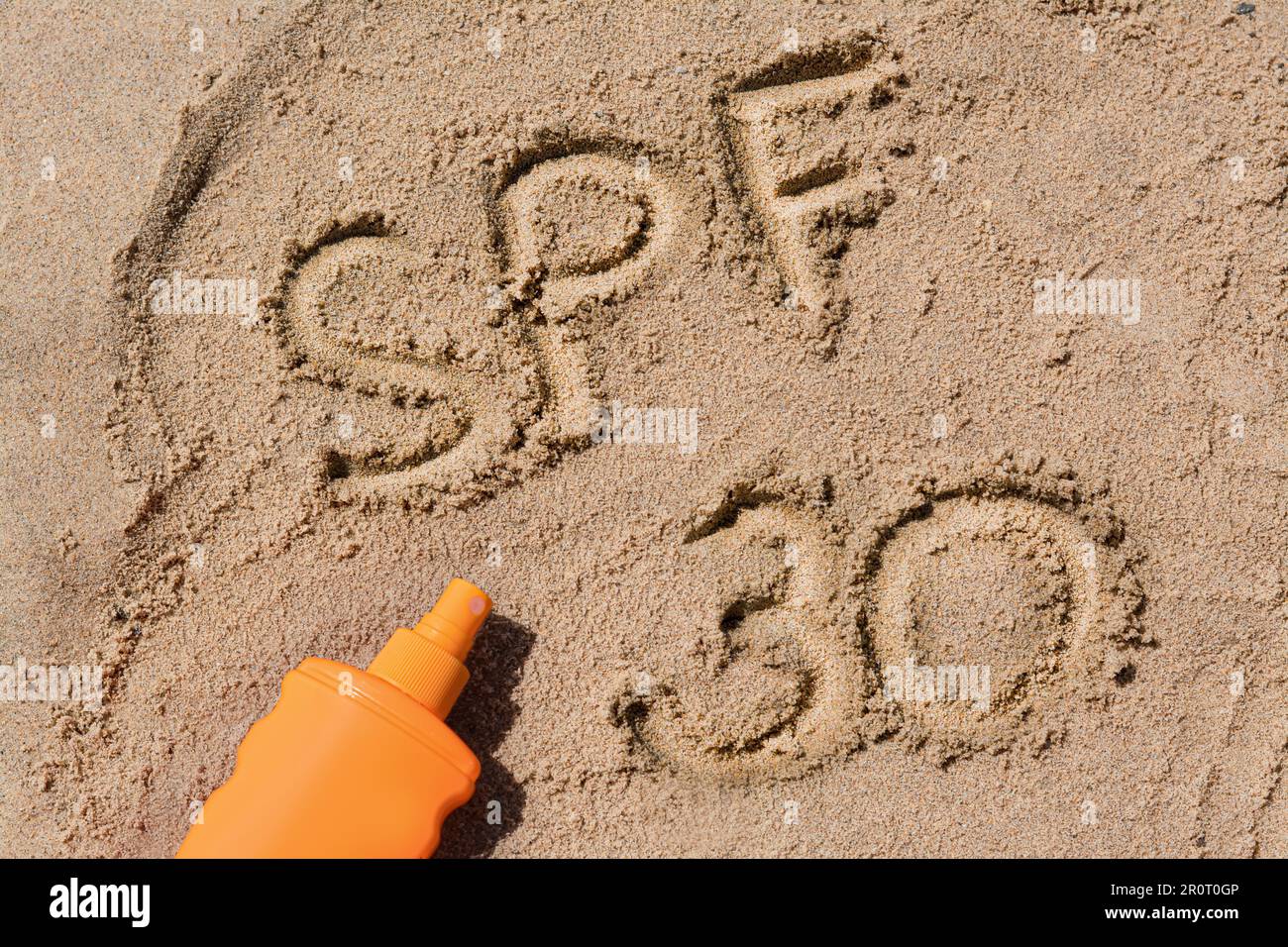 Abbreviation SPF 30 written on sand and bottle of sunscreen at beach ...