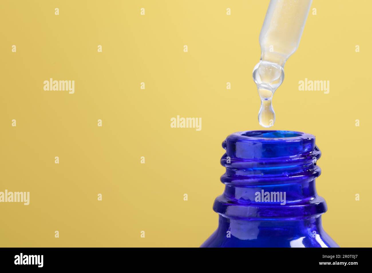 Dripping serum from pipette into bottle on yellow background, closeup ...