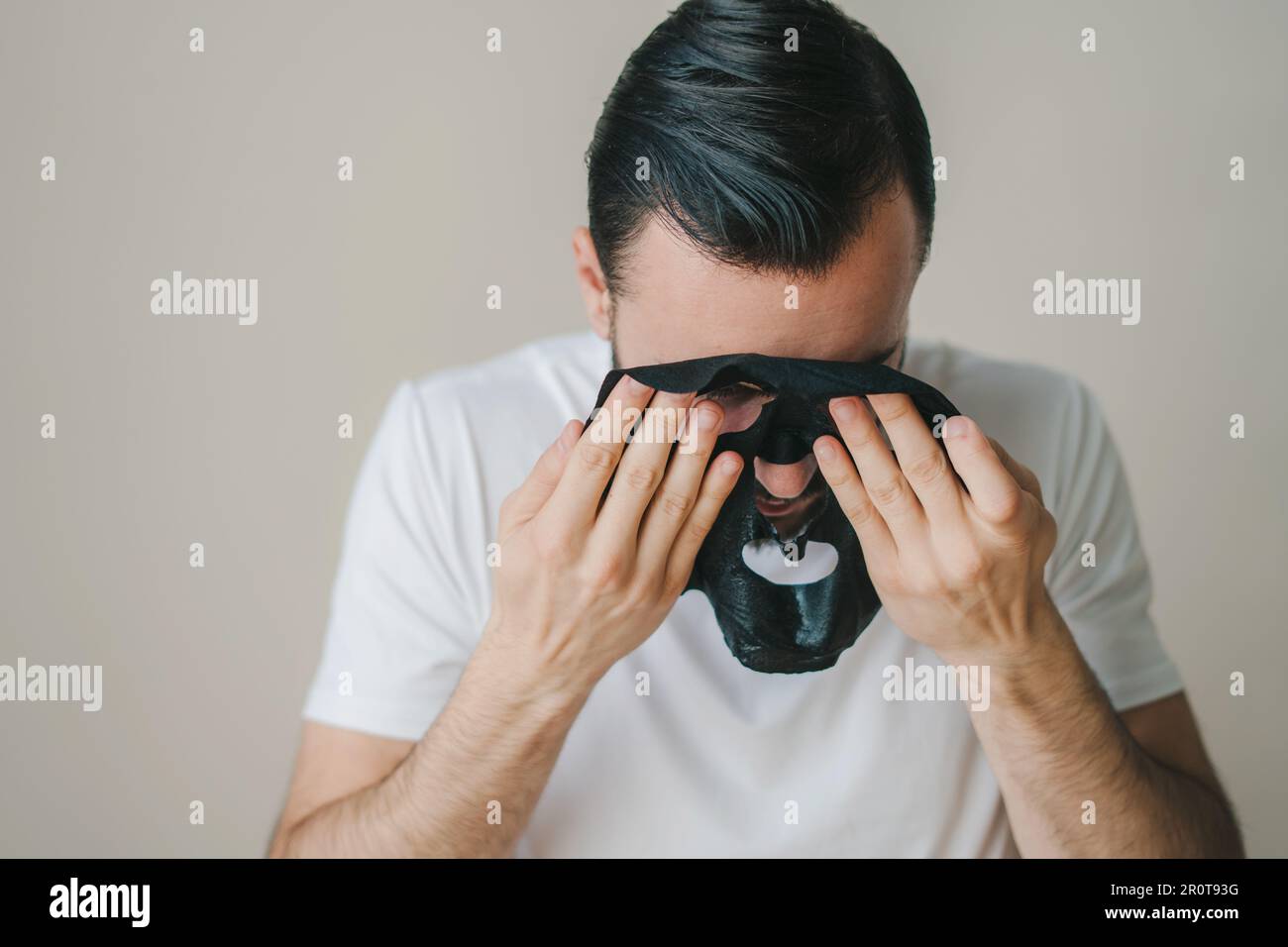 Portrait of a young man peeling off a black facial mask isolated over ...