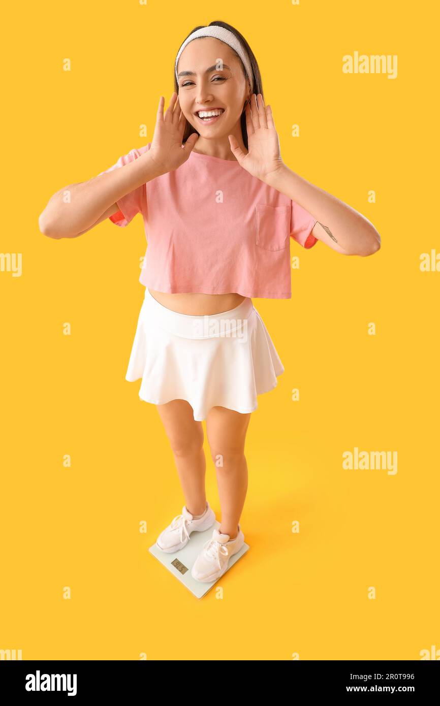 Young woman measuring her weight on scales against yellow background ...