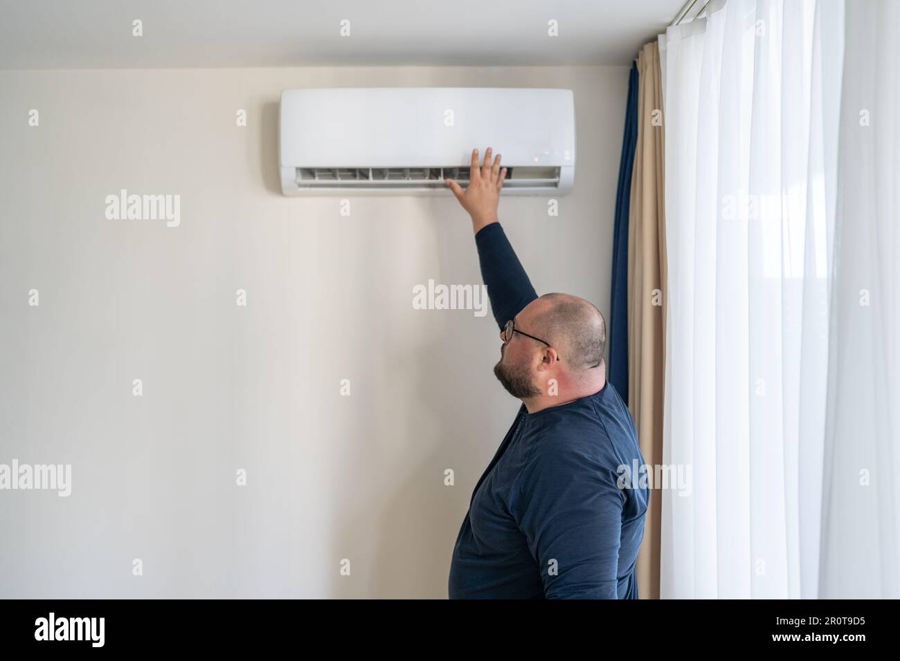 Man checking working air conditioner touching air by hand in summer hot ...