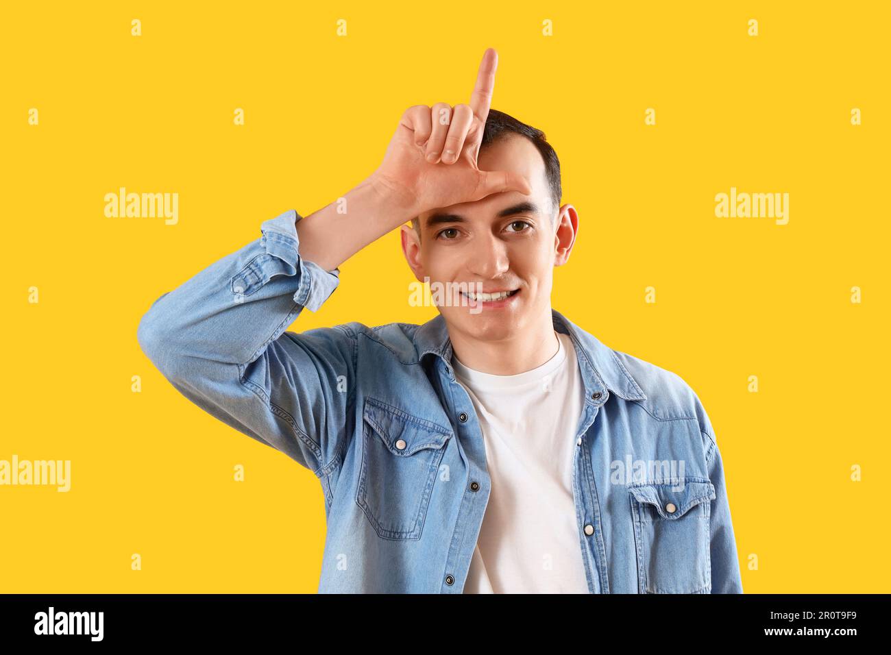 Young man showing loser gesture on yellow background Stock Photo - Alamy