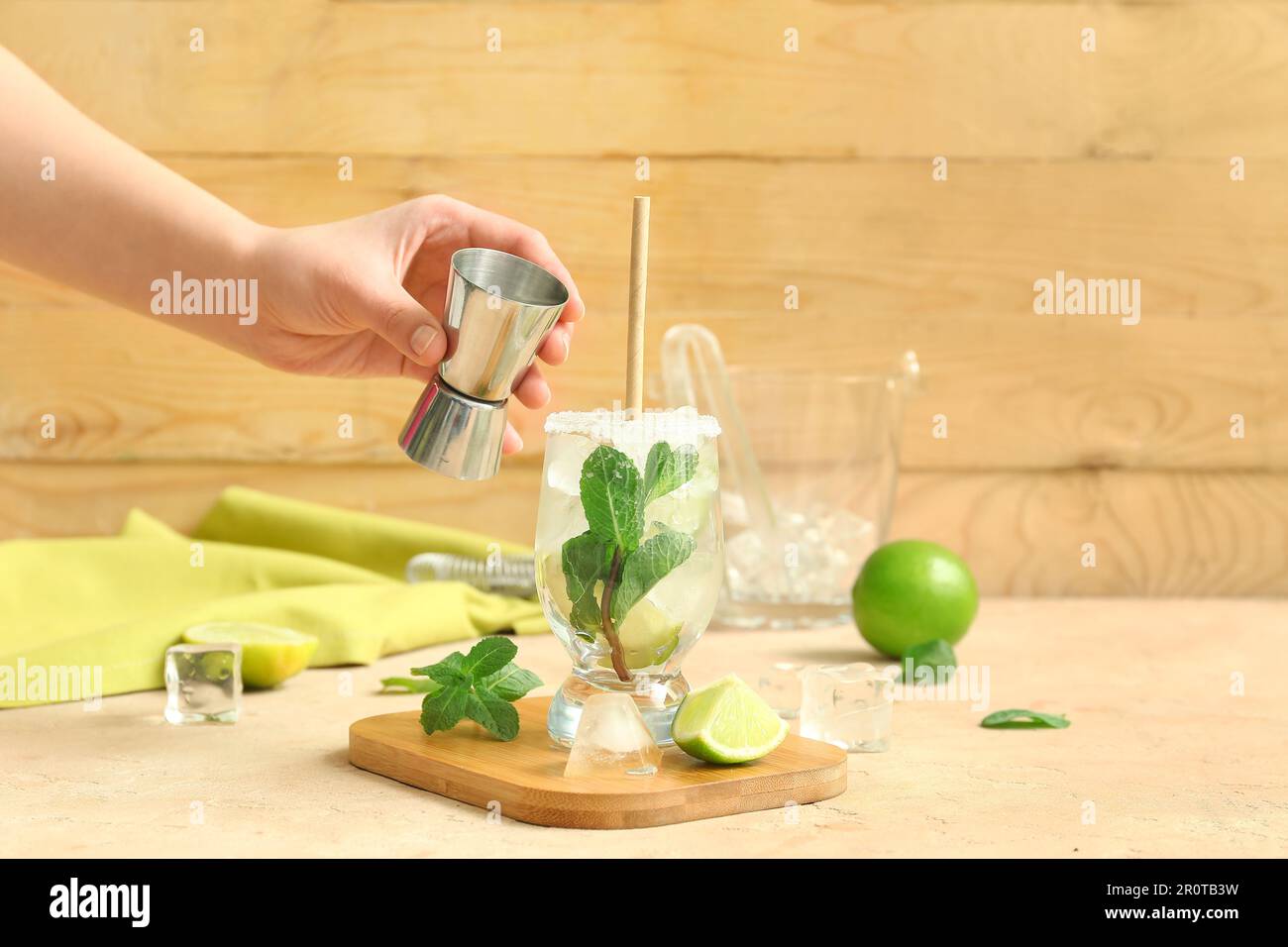 Female bartender making tasty mojito cocktail on table near wooden wall ...