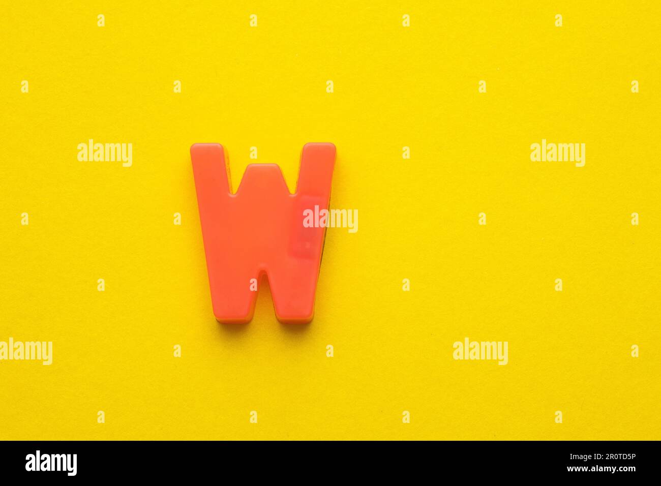 Peach colored plastic letter W uppercase on yellow foamy background ...