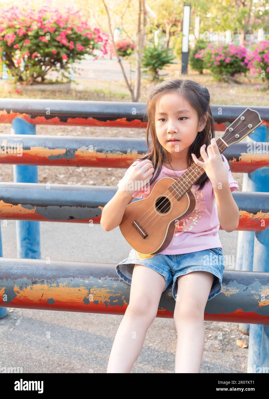 Little asian child girl play the ukulele, in the garden on the Steel ...