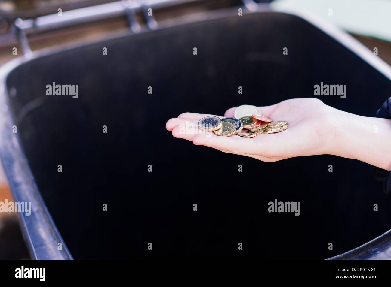 A kid girl hand throws euro coins into a trash can dumpster, street ...