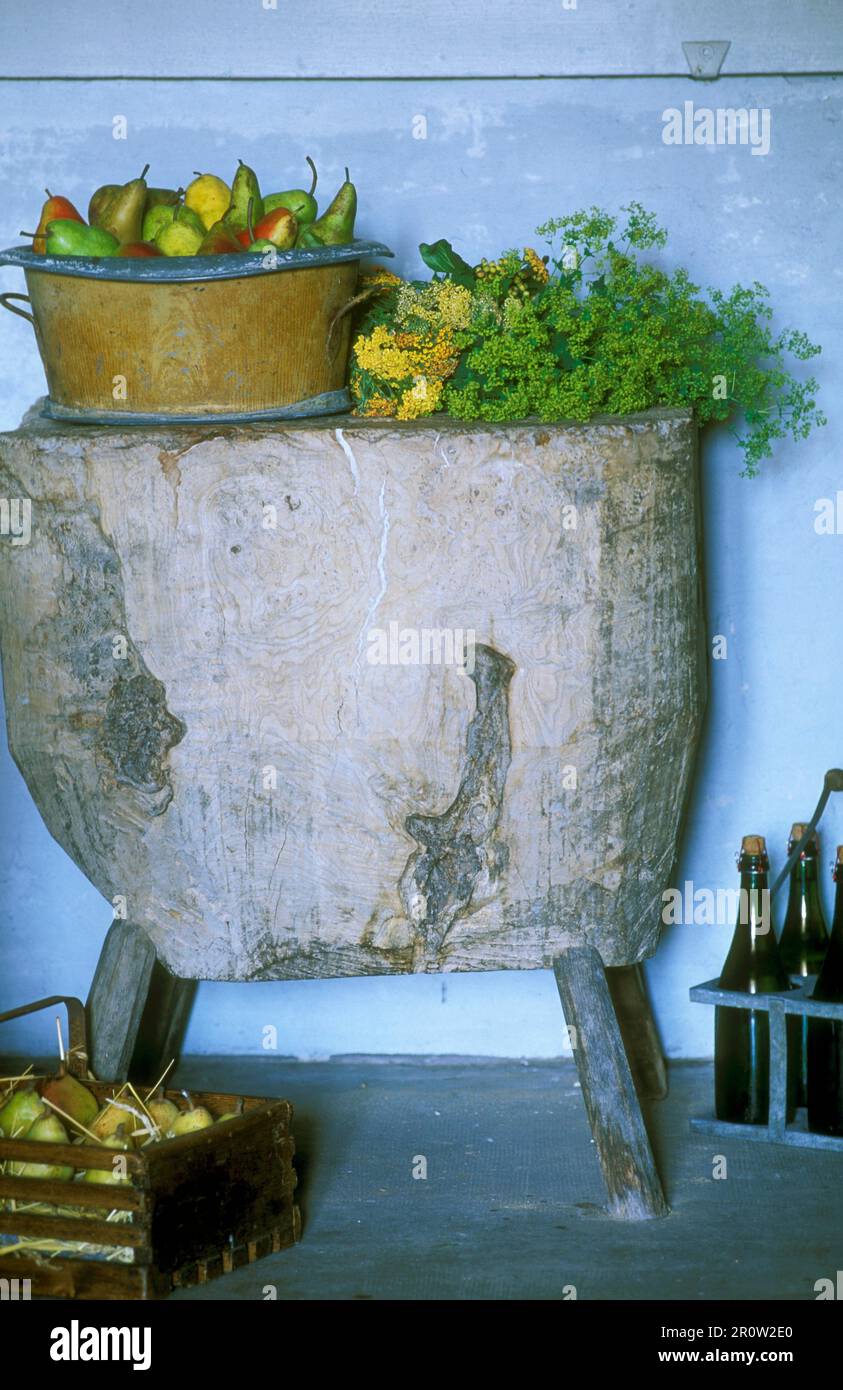 Pears in a bowl on a rustic wooded block next to a carrier with bottles ...