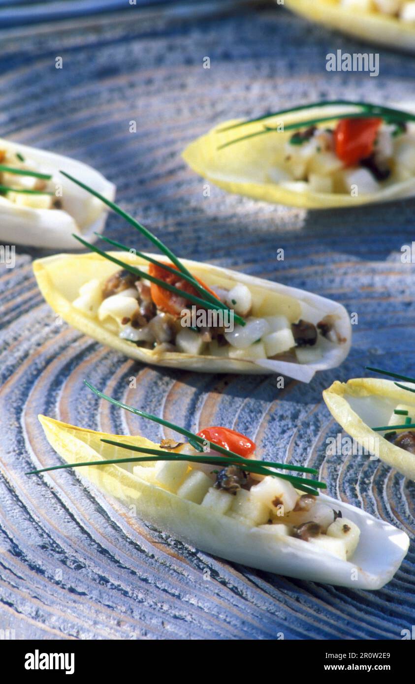 Chicory boats with scallops, green apple and chives on a blue surface ...