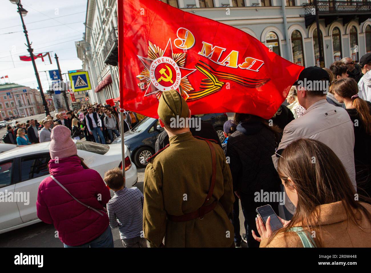A boy stands at a pedestrian crossing with a flag of Soviet symbols and ...