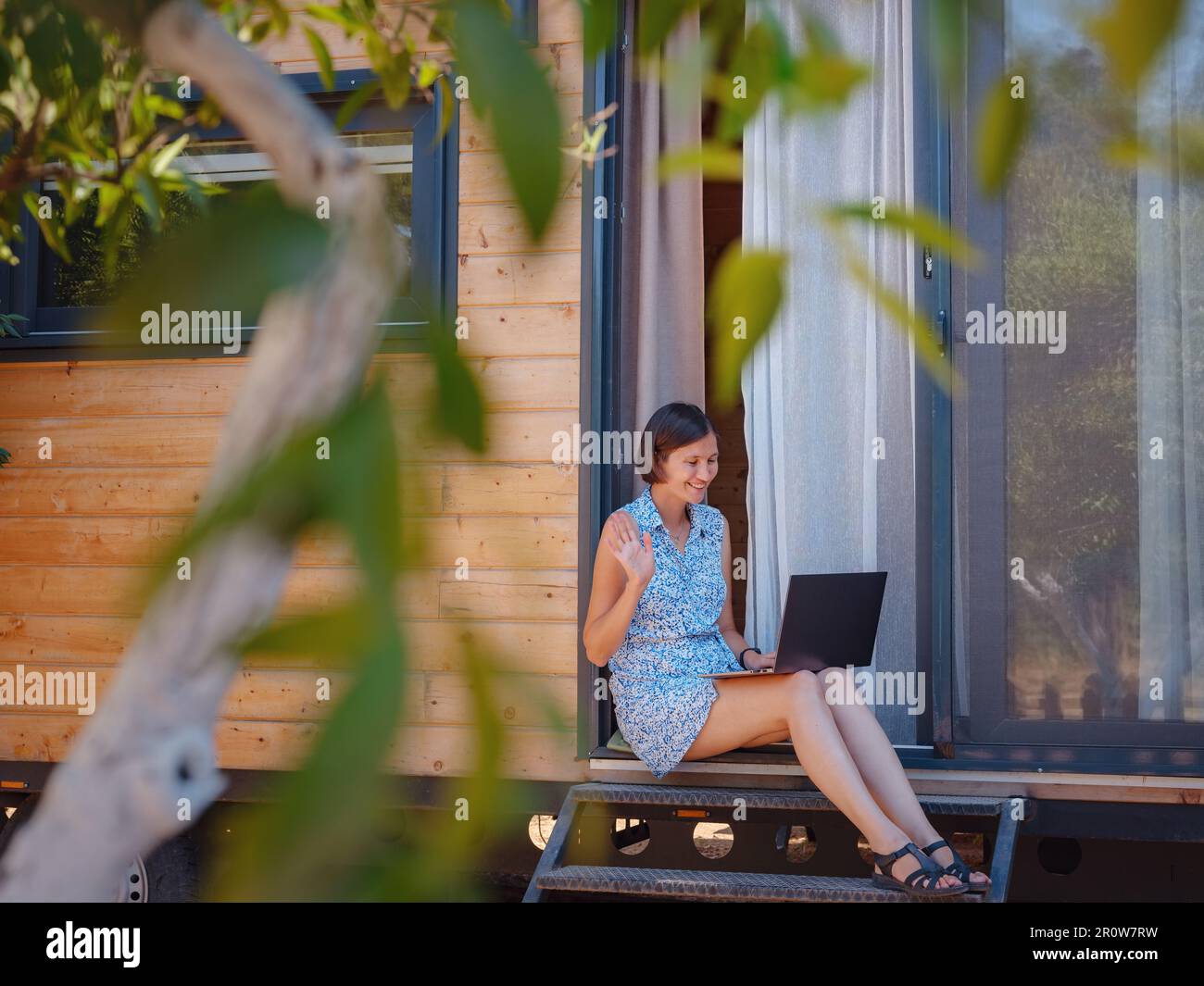 Happy young asian woman with laptop resting outdoors near tiny house ...