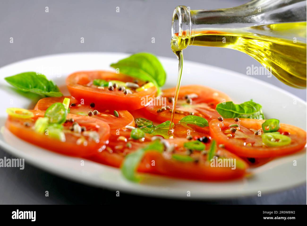 Pouring olive oil onto a tomato and basil salad Stock Photo - Alamy