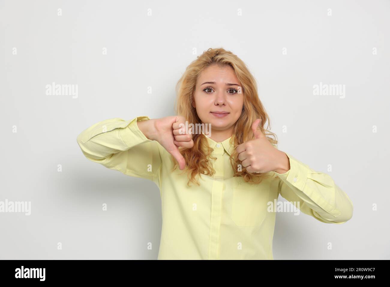 Conflicted young woman showing thumbs up and down gestures on white ...