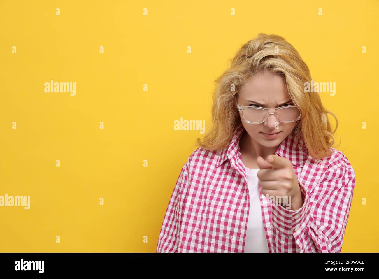 Aggressive young woman pointing on yellow background. Space for text ...
