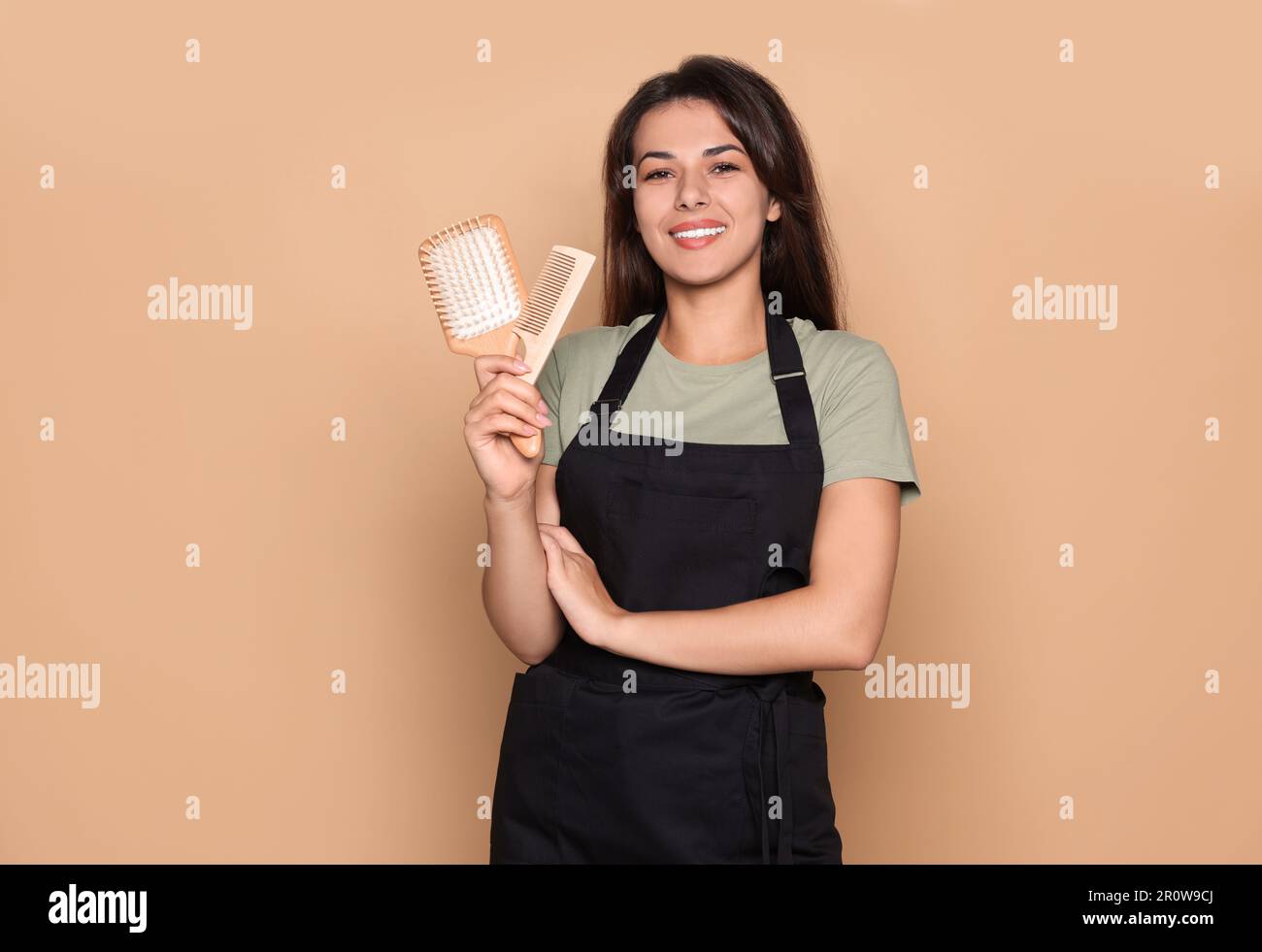 Happy professional hairdresser in apron with hairbrush and comb against ...
