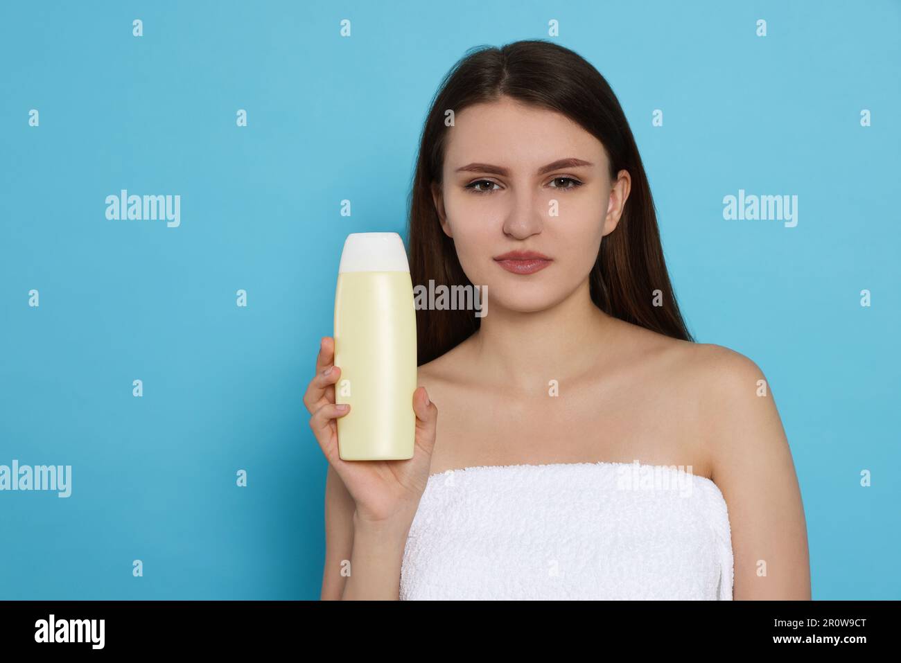 Beautiful young woman wrapped in towel holding bottle of shampoo on ...