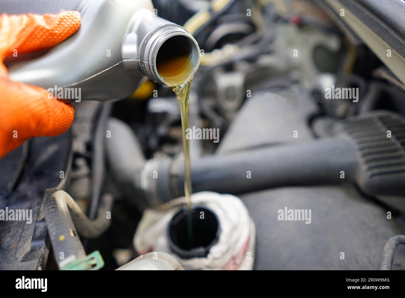Pouring oil to the car. Car mechanic holding a bottle of oil in hand ...
