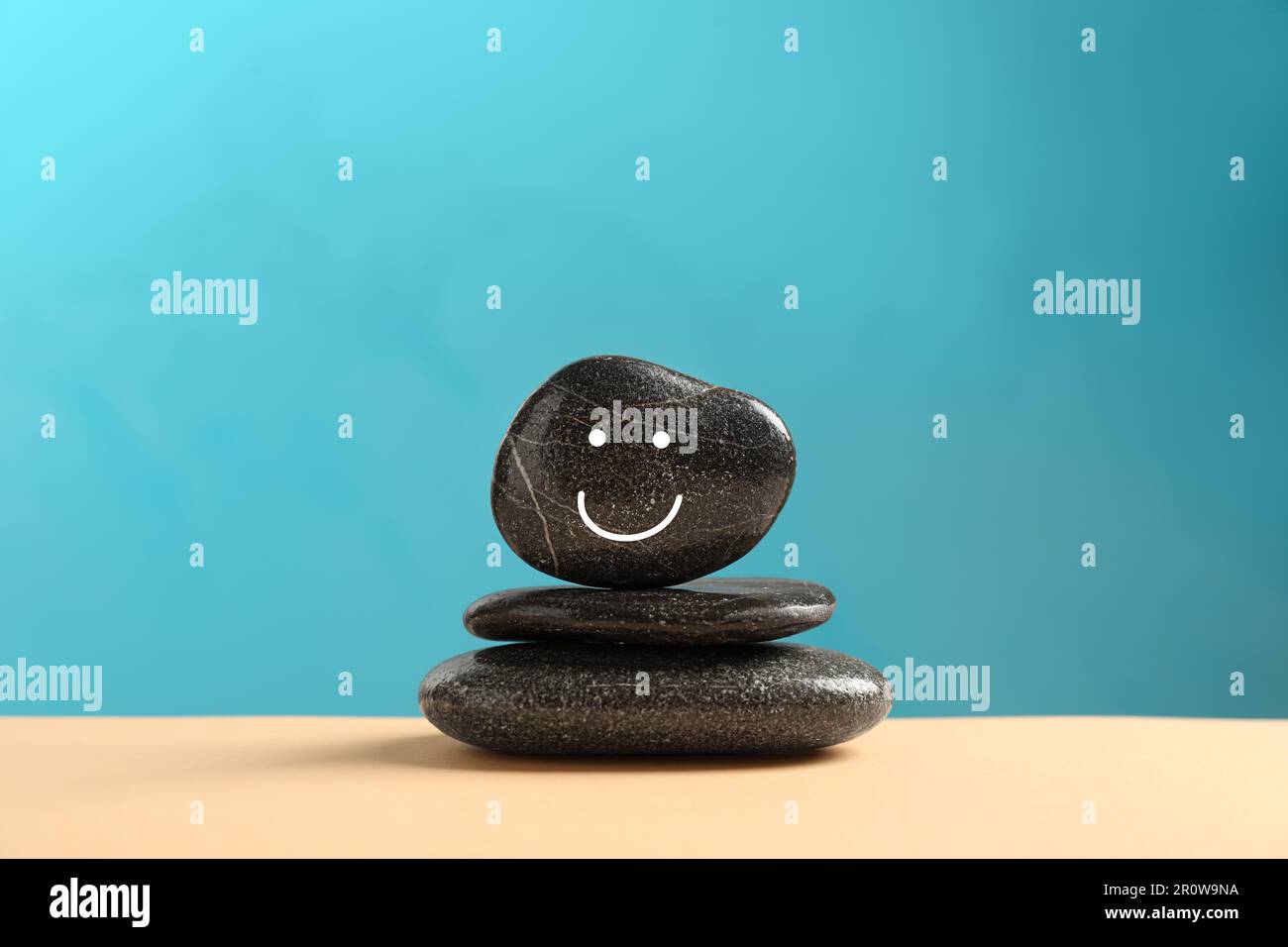 Stack of stones with drawn happy face on beige table against light blue ...