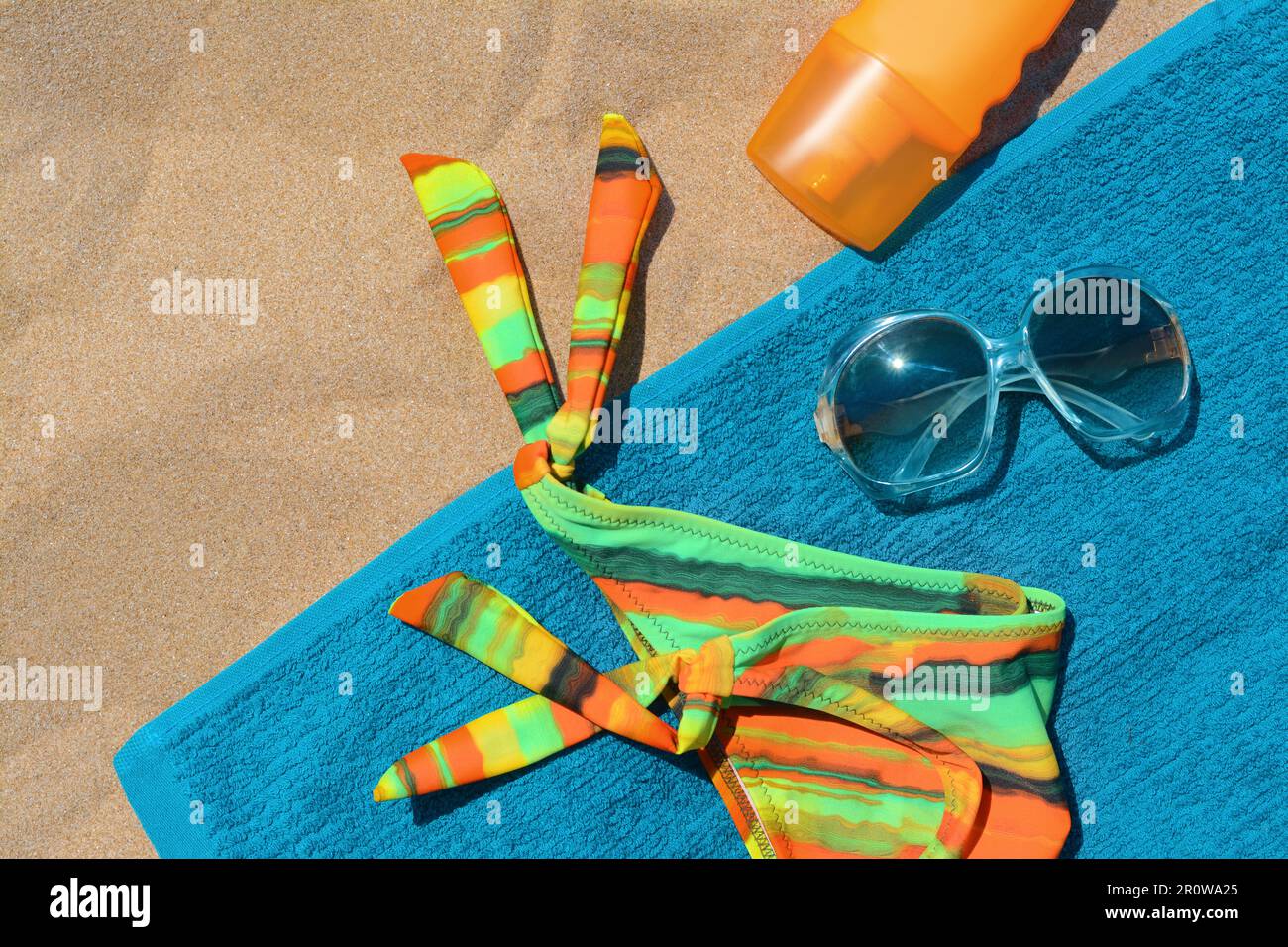 Soft blue beach towel with bottle of sunscreen, sunglasses and colorful ...