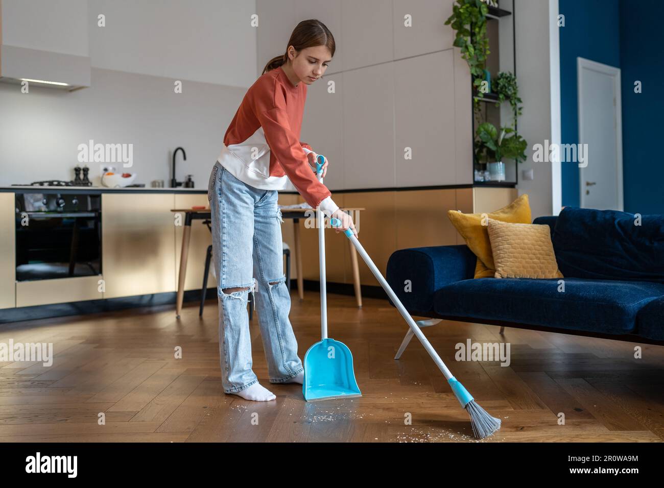 Teen girl doing chores cleaning floor in kitchen sweeping trash with ...