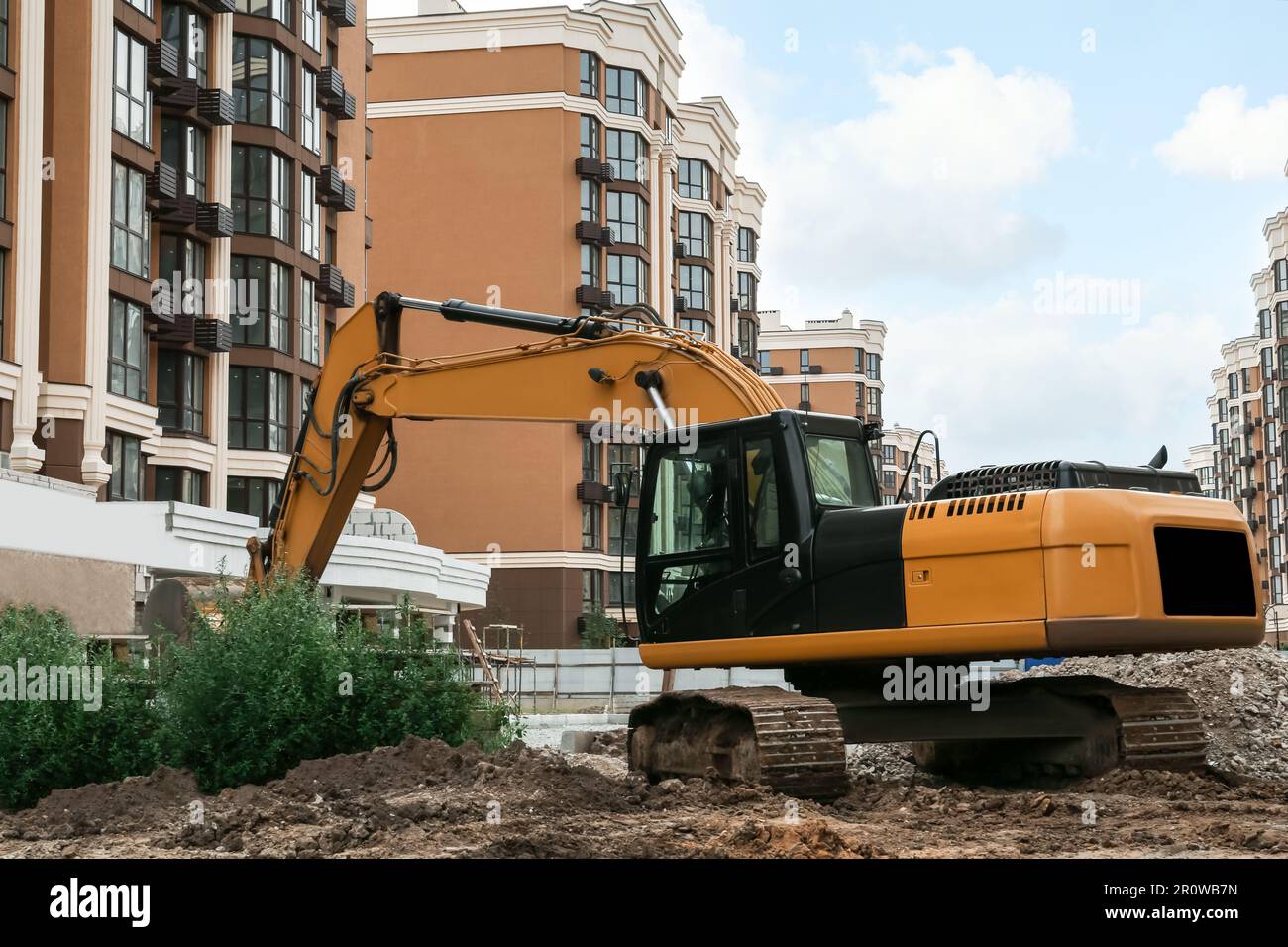 Modern excavator near buildings on construction site Stock Photo - Alamy