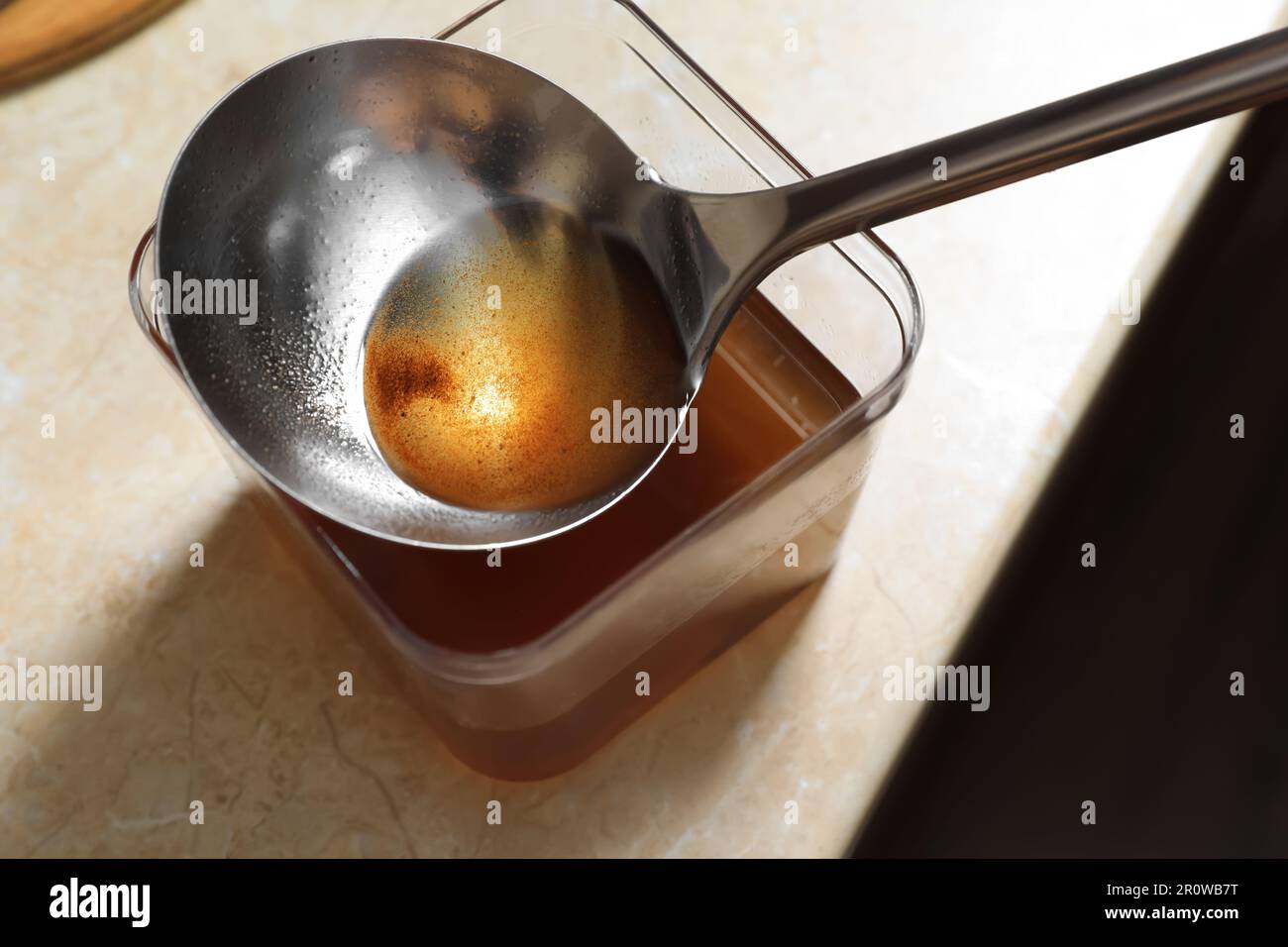Container and ladle with used cooking oil on beige table Stock Photo ...