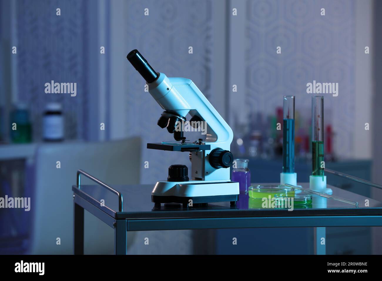 Modern microscope and glassware with colorful liquids on metal table in ...