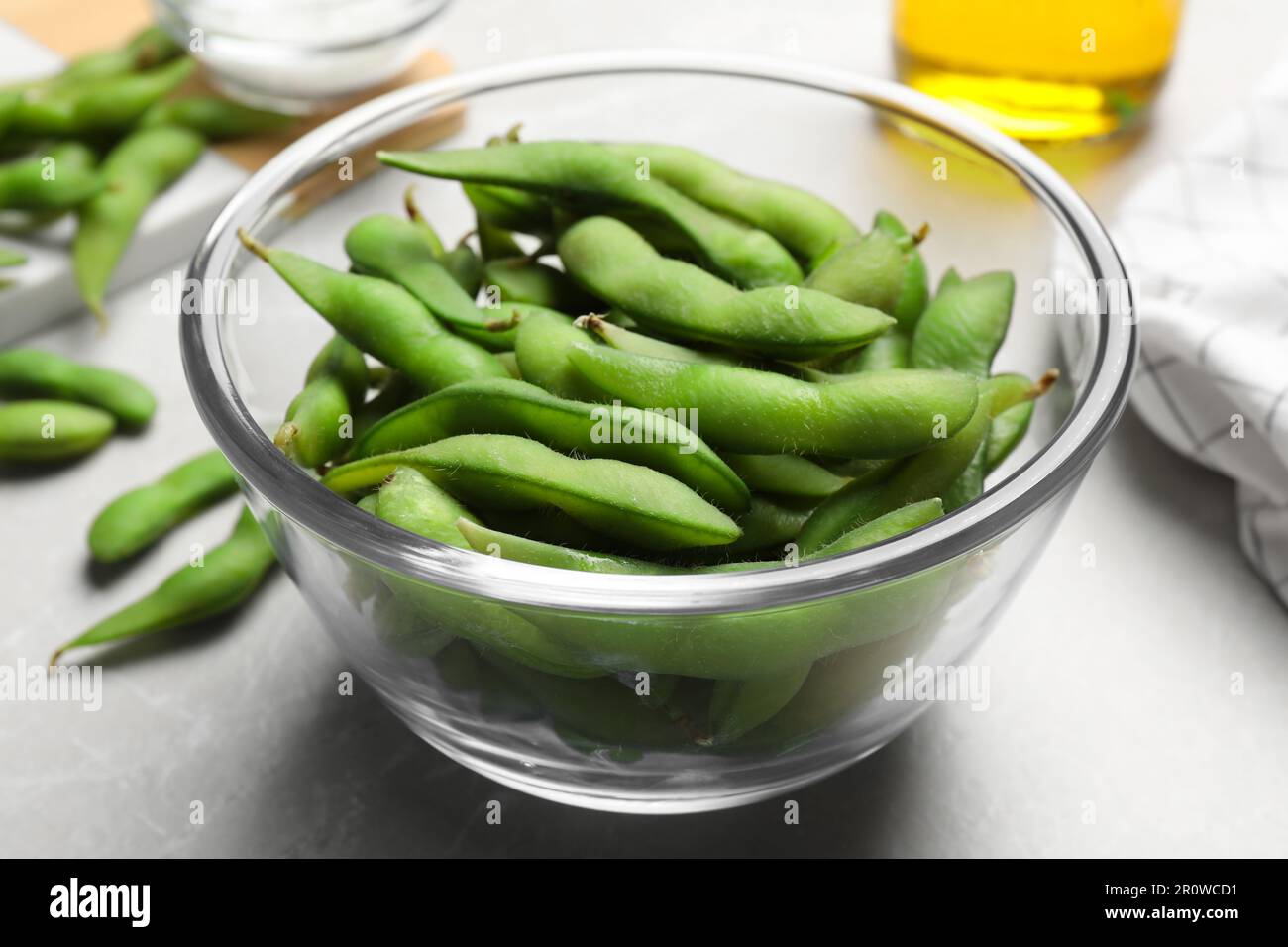 Bowl with green edamame beans in pods on light grey table, closeup ...