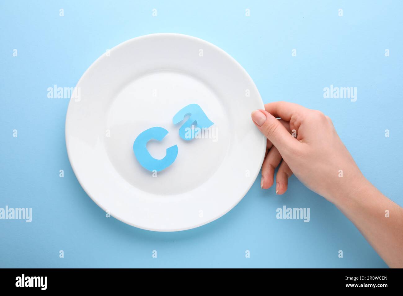 Woman holding plate with calcium symbol made of letters on light blue ...