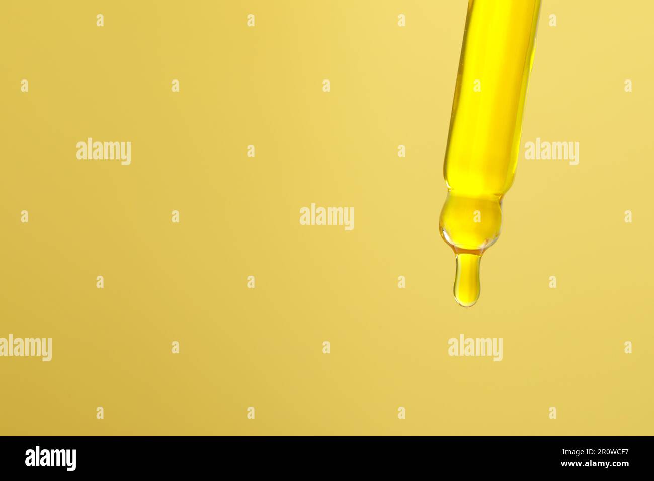 Dripping serum from pipette on yellow background, closeup. Space for ...