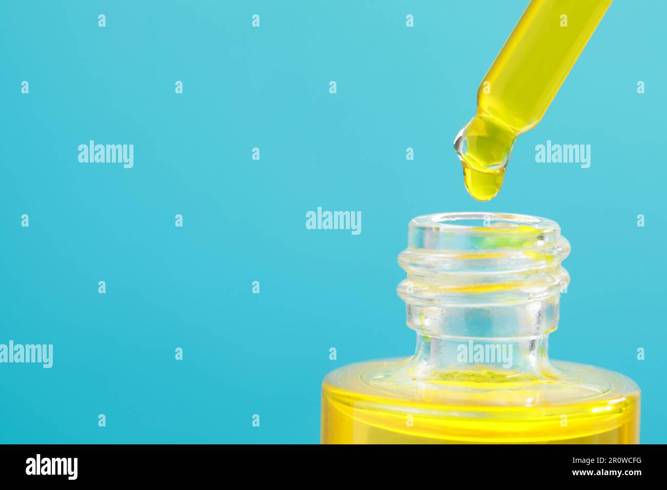 Dripping yellow serum from pipette into bottle on light blue background ...