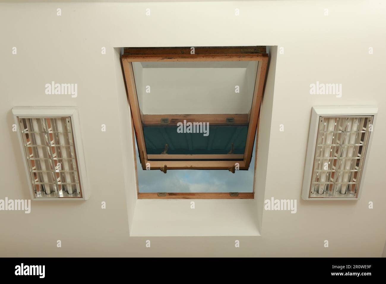 Open skylight roof window on slanted ceiling in attic room, bottom view ...