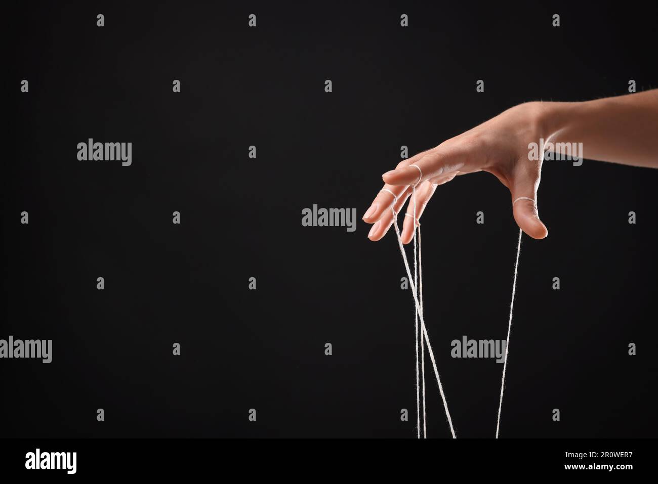 Woman pulling strings of puppet on black background, closeup. Space for ...