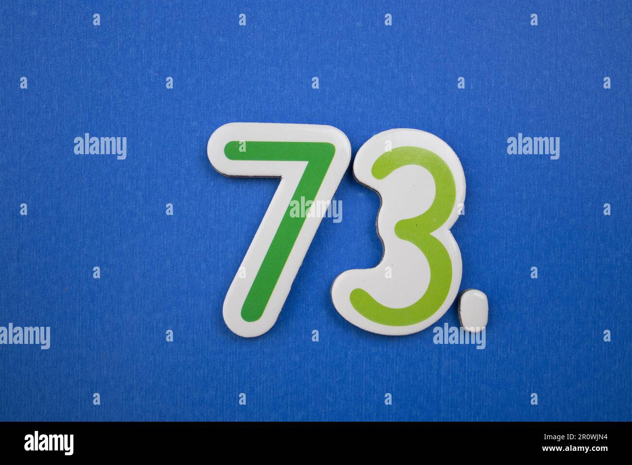 The number 73 in green color, photographed from above, placed on a blue ...