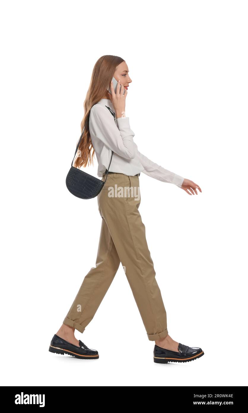 Young woman talking on smartphone while walking against white ...