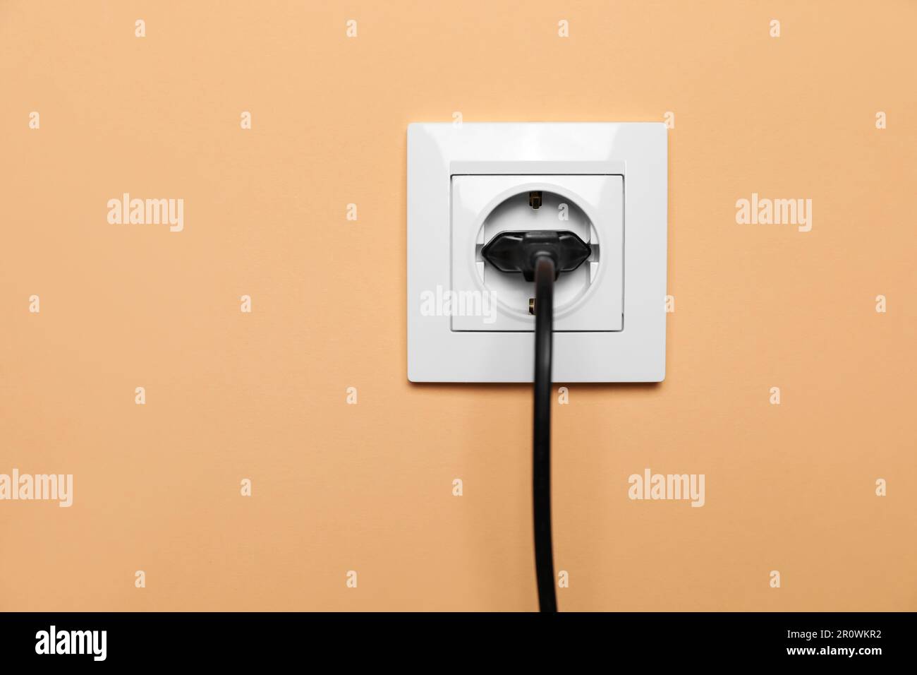 Power socket with inserted plug on pale orange wall. Electrical supply ...