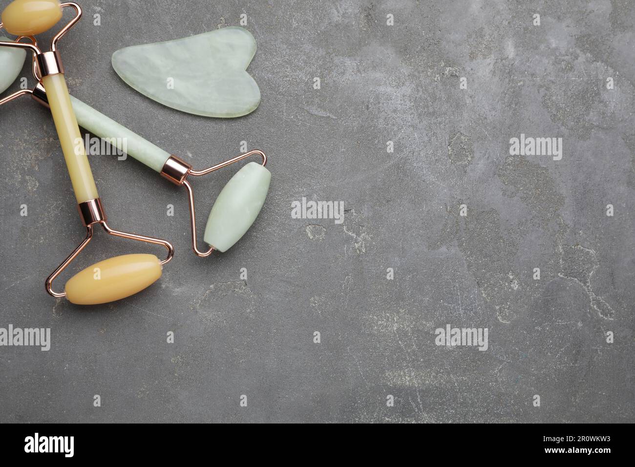 Gua sha stone and different face rollers on grey table, flat lay. Space ...