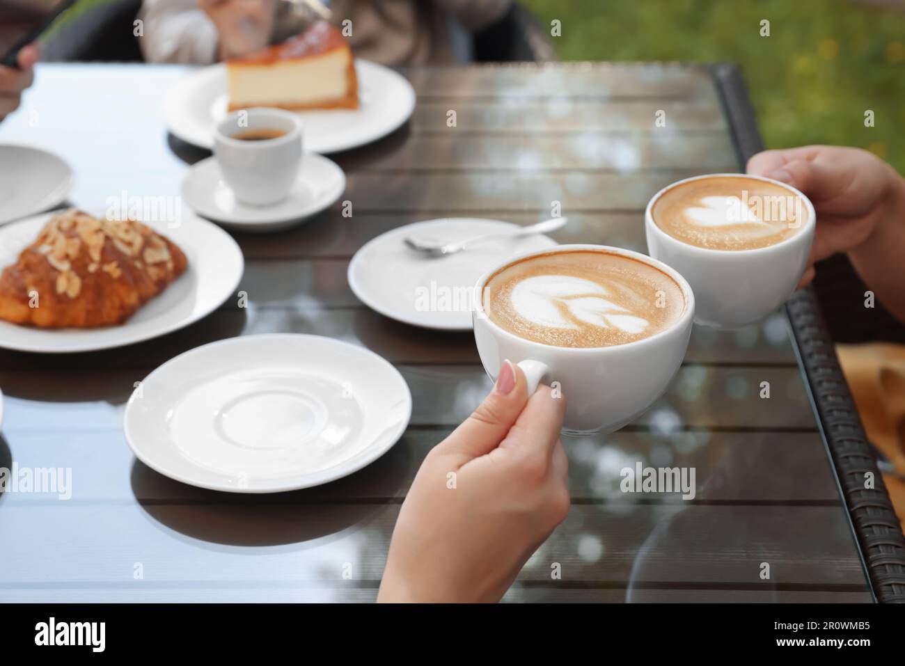 Friends drinking coffee at wooden table in outdoor cafe, closeup Stock ...