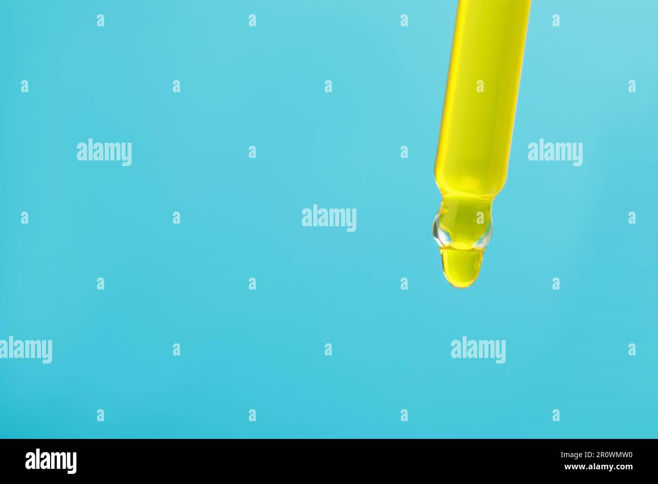 Dripping yellow serum from pipette on light blue background, closeup ...